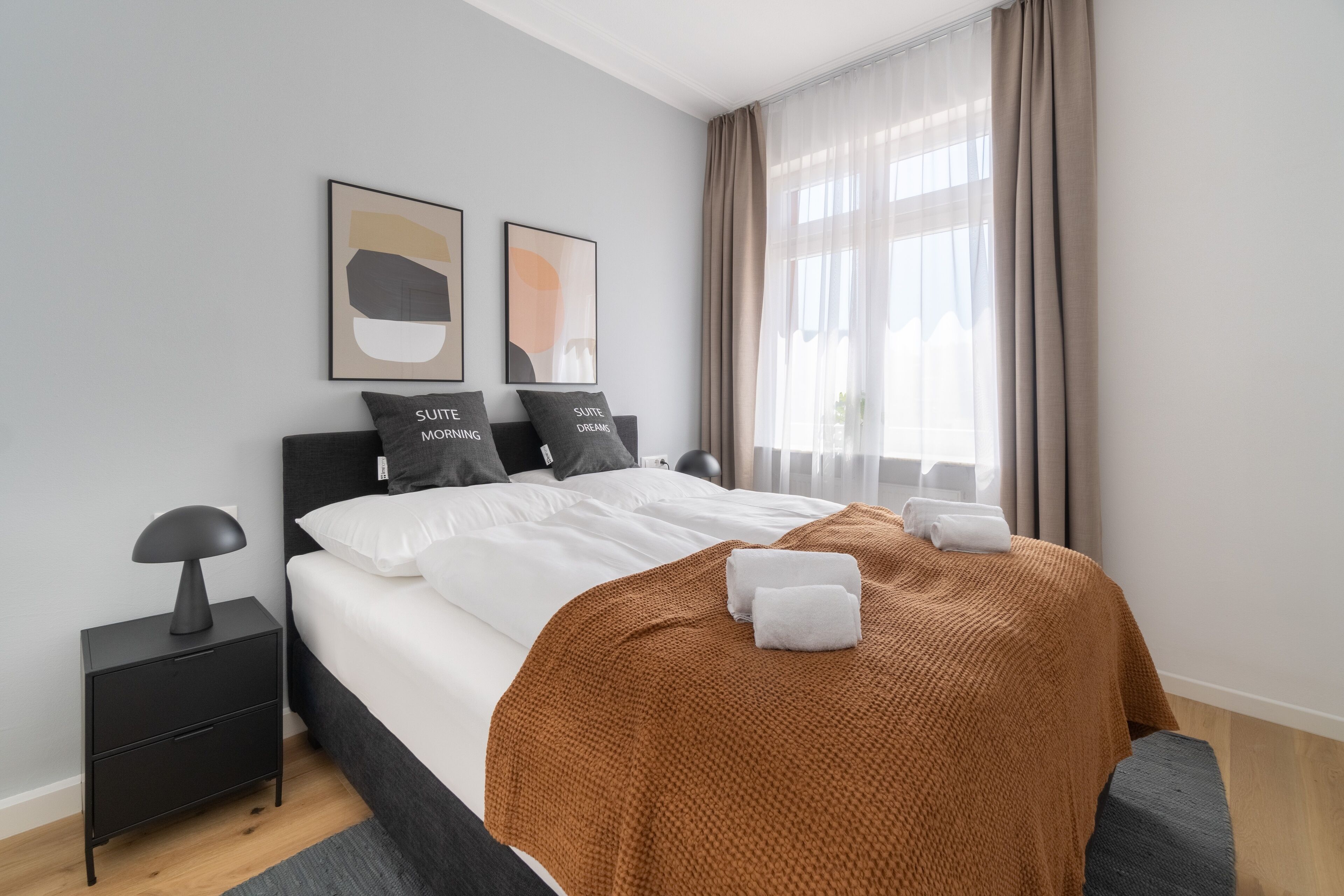 Quarto moderno com cama, mesa de cabeceira e uma obra de arte na parede.