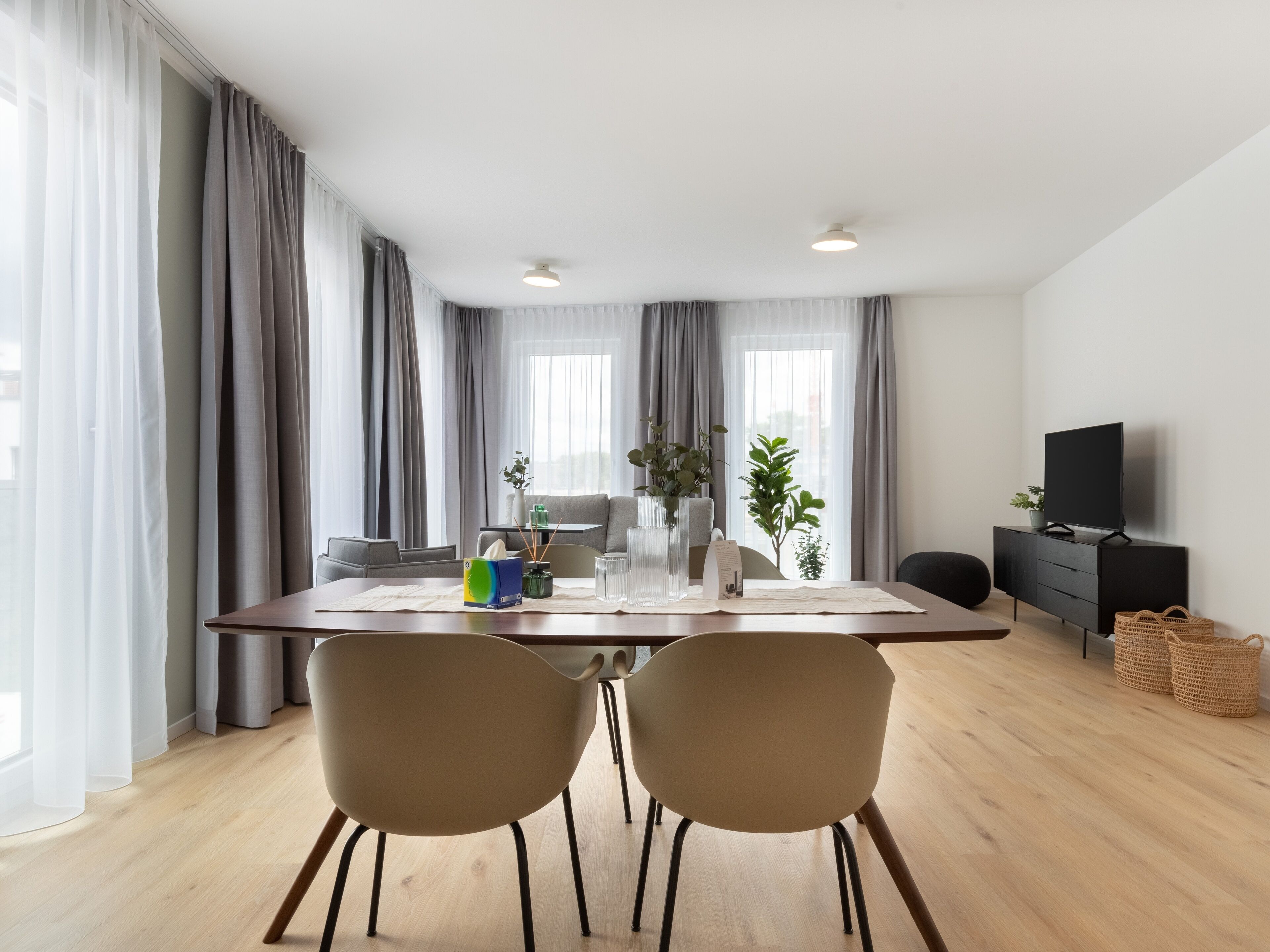 Uma sala de estar moderna com uma mesa de jantar, duas cadeiras, um sofá, uma televisão e uma planta.