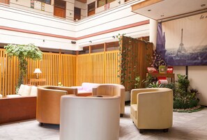 Um hall espaçoso com teto alto, destacando uma área de estar com sofás e poltronas, um painel de madeira com vegetação e um grande pôster da Torre Eiffel.