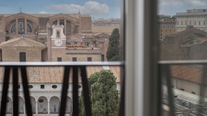 Vista de um edifício histórico com torre de relógio, janelas em arco e um pátio com colunas.