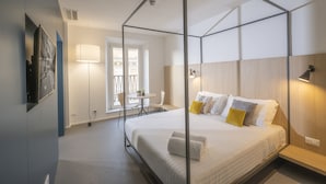 Quarto moderno com cama de dossel, uma pequena mesa com cadeiras, uma luminária e vista para o exterior.