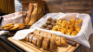 Diversos pães e doces expostos em um balcão de madeira.