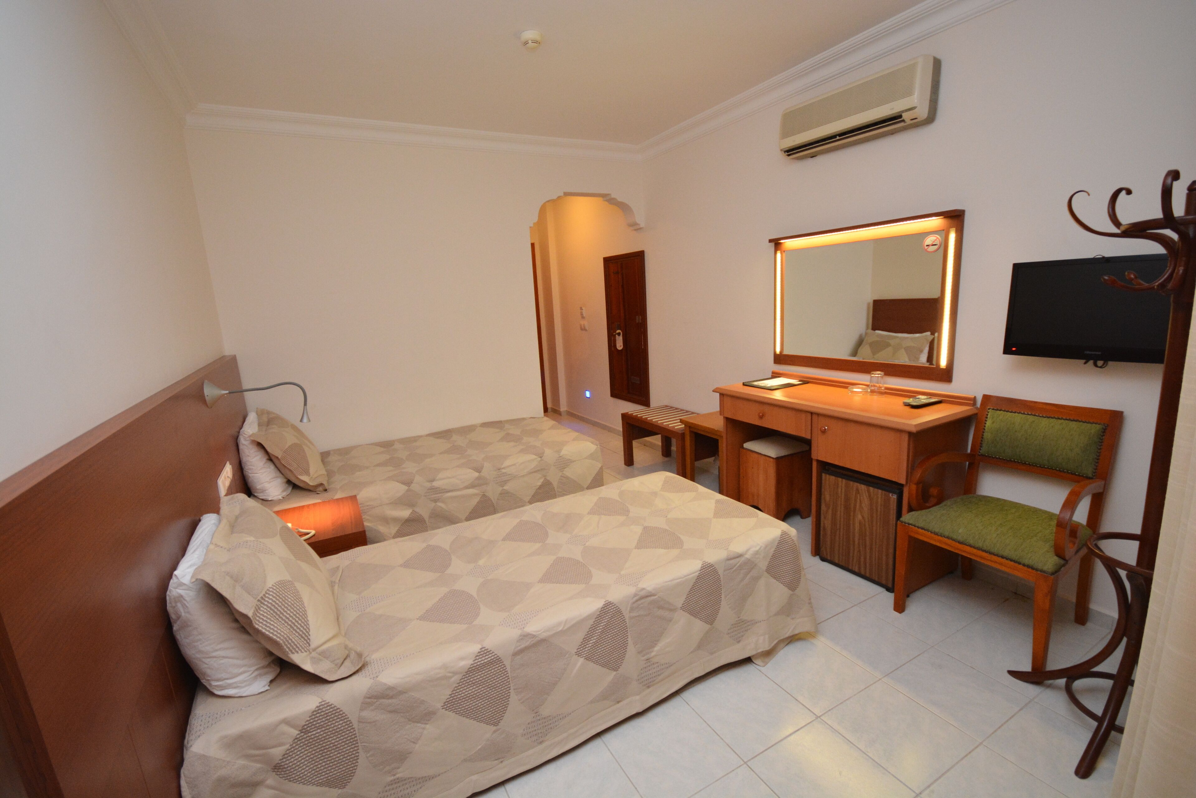 Quarto de hotel com duas camas, uma escrivaninha, uma cadeira, uma televisão e aparelho de ar condicionado.