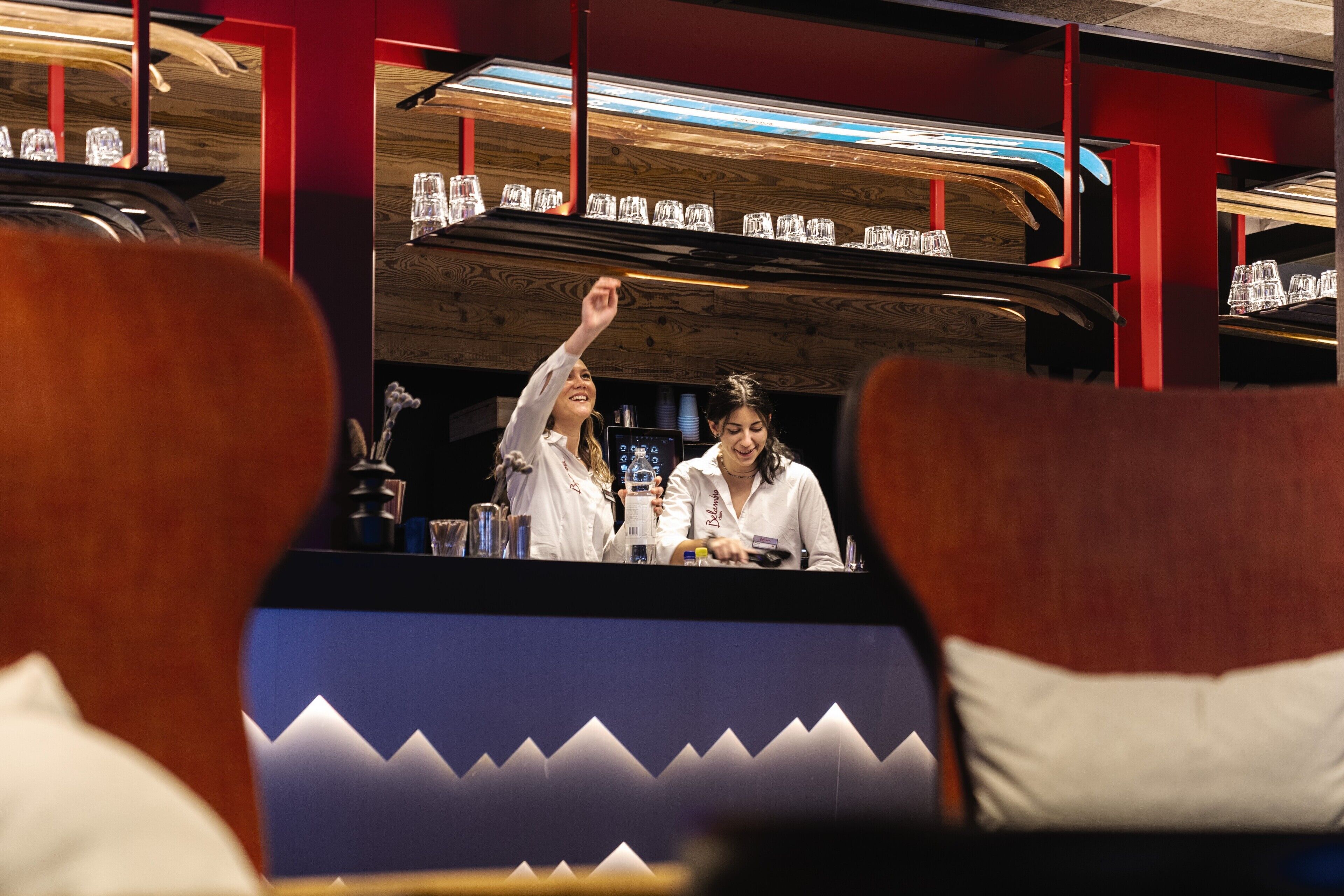 Uma área de bar com teto de madeira e detalhes vermelhos, apresentando um balcão e estantes com copos.