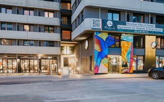 Um edifício com um mural colorido na fachada, um anúncio de apartamentos para estudantes e profissionais, e um código QR.