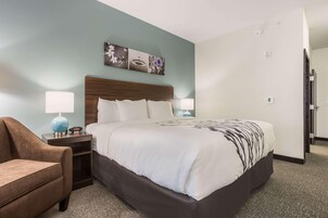 Quarto de hotel com cama, mesa de cabeceira, abajur e uma cadeira.