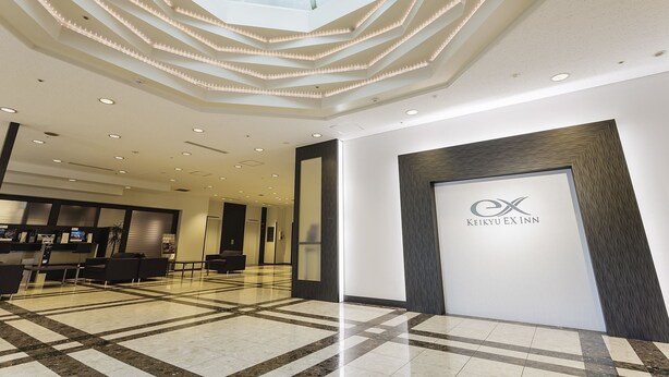 Um saguão de hotel com design moderno, apresentando um padrão de piso xadrez, uma área de estar central e uma recepção bem visível com o nome do hotel.