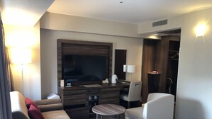 Quarto de hotel com cama, escrivaninha, cadeira, televisão e guarda-roupa.