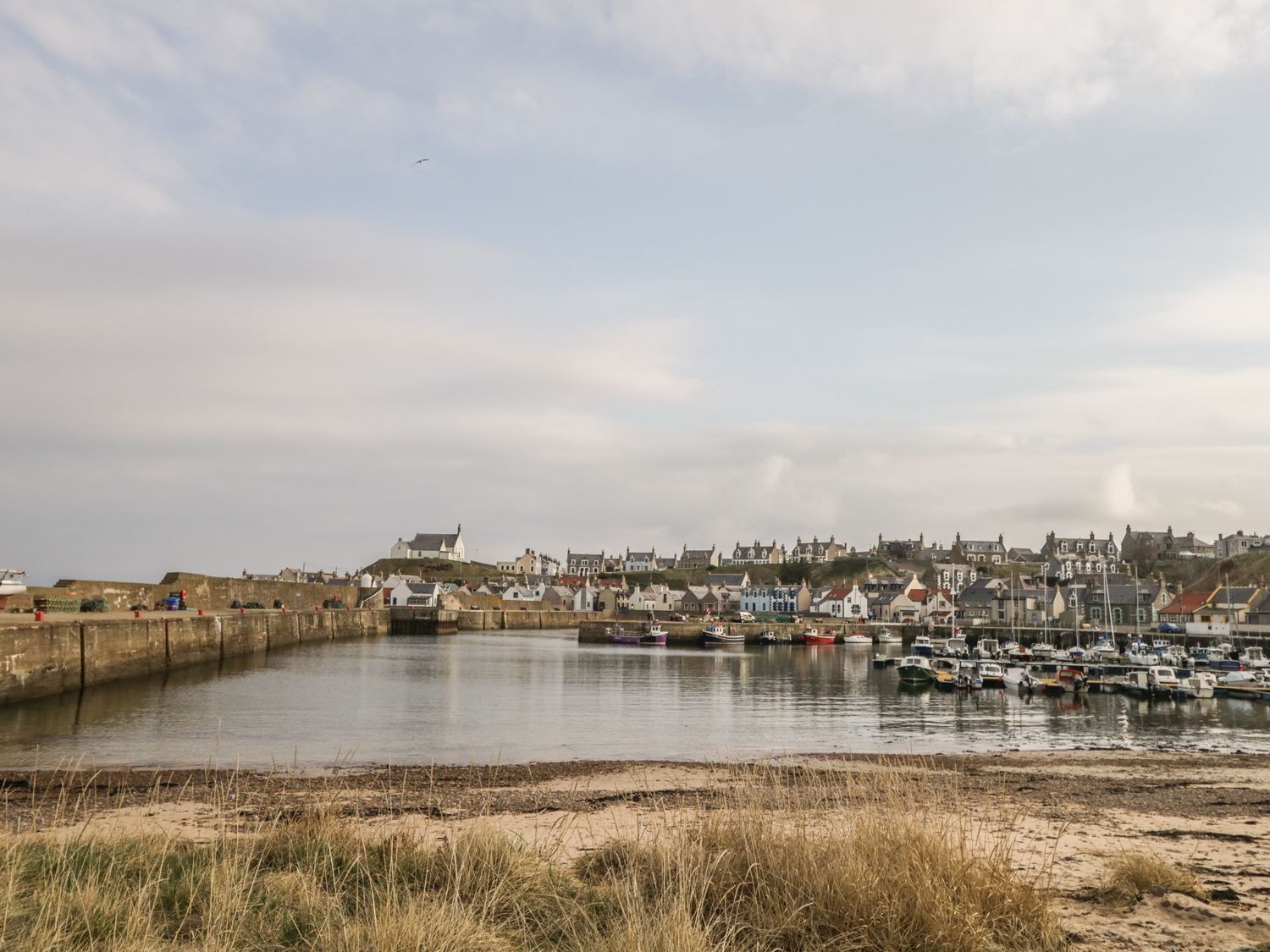 Uma vila costeira com um porto cheio de barcos, uma praia de areia e um cenário de edifícios históricos.