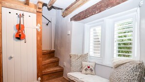 Uma escadaria leva a um quarto com janela, um violino pendurado na parede e um banquinho estofado com almofadas.