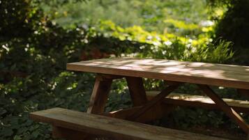 Uma mesa de piquenique de madeira com bancos numa área de jardim arborizada.