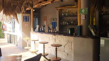 Uma área de bar com balcão de pedra, banquetas e diversos copos e garrafas.