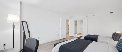 Quarto de hotel com uma cama, uma escrivaninha, uma cadeira e um abajur.