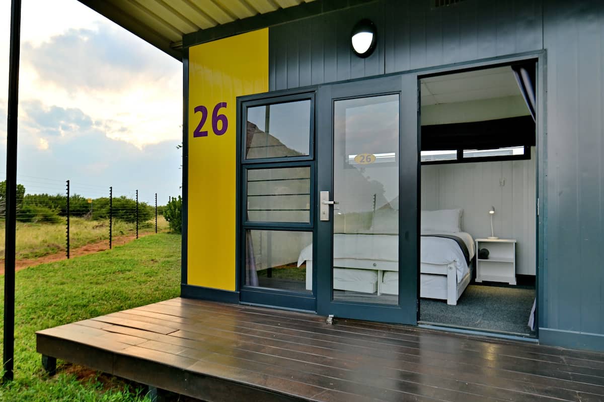 Um edifício moderno com o número '26' na fachada, um deck de madeira e um quarto com cama e mesa de cabeceira.
