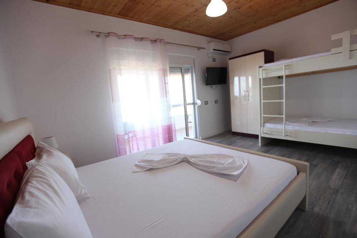 Quarto com uma cama de solteiro, uma cama beliche, um guarda-roupa e uma televisão na parede.
