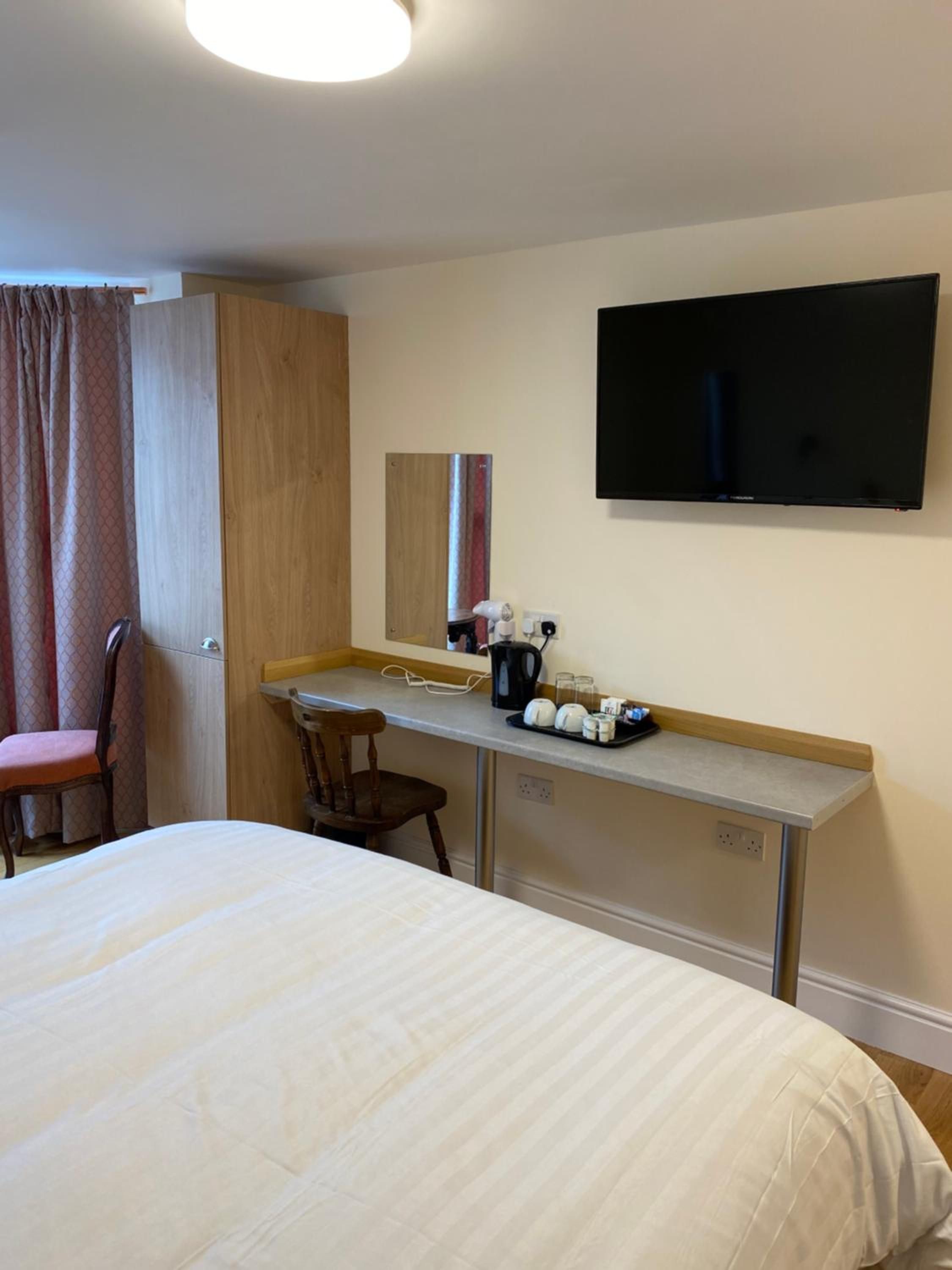 Quarto de hotel com cama, escrivaninha, televisão de tela plana, cadeira, pequeno espaço de cozinha e guarda-roupa.