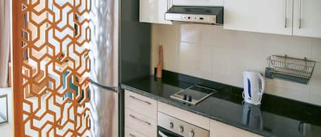 Uma cozinha moderna com frigorífico em aço inoxidável, forno embutido e bancada preta.