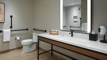 Uma casa de banho moderna com sanita branca, lavatório com espelho e barra de apoio.