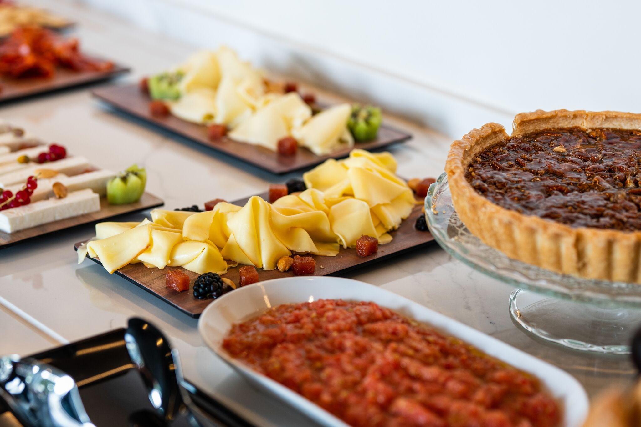 Buffet com diversos pratos, incluindo torta, queijo e frutas.