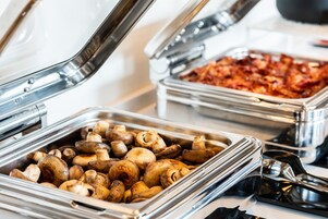 Buffet com diversos alimentos, incluindo cogumelos e um prato que parece ser de bacon.
