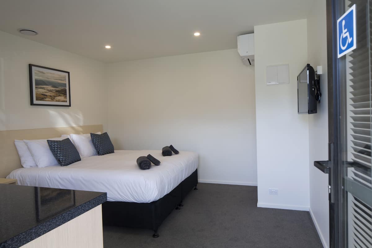 Quarto de hotel com cama, mesa, televisão e identificação de acessibilidade para cadeiras de rodas.