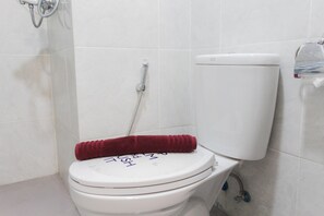 Sanitário branco com uma toalha vermelha em cima e um chuveiro fixado na parede.