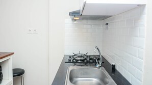 Cozinha compacta com fogão a gás, pia de aço inoxidável e painel de azulejos branco.