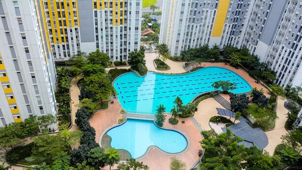 Piscina cercada por vegetação e edifícios altos.
