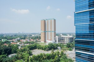 Um edifício alto com design moderno, rodeado por vegetação e outros edifícios.