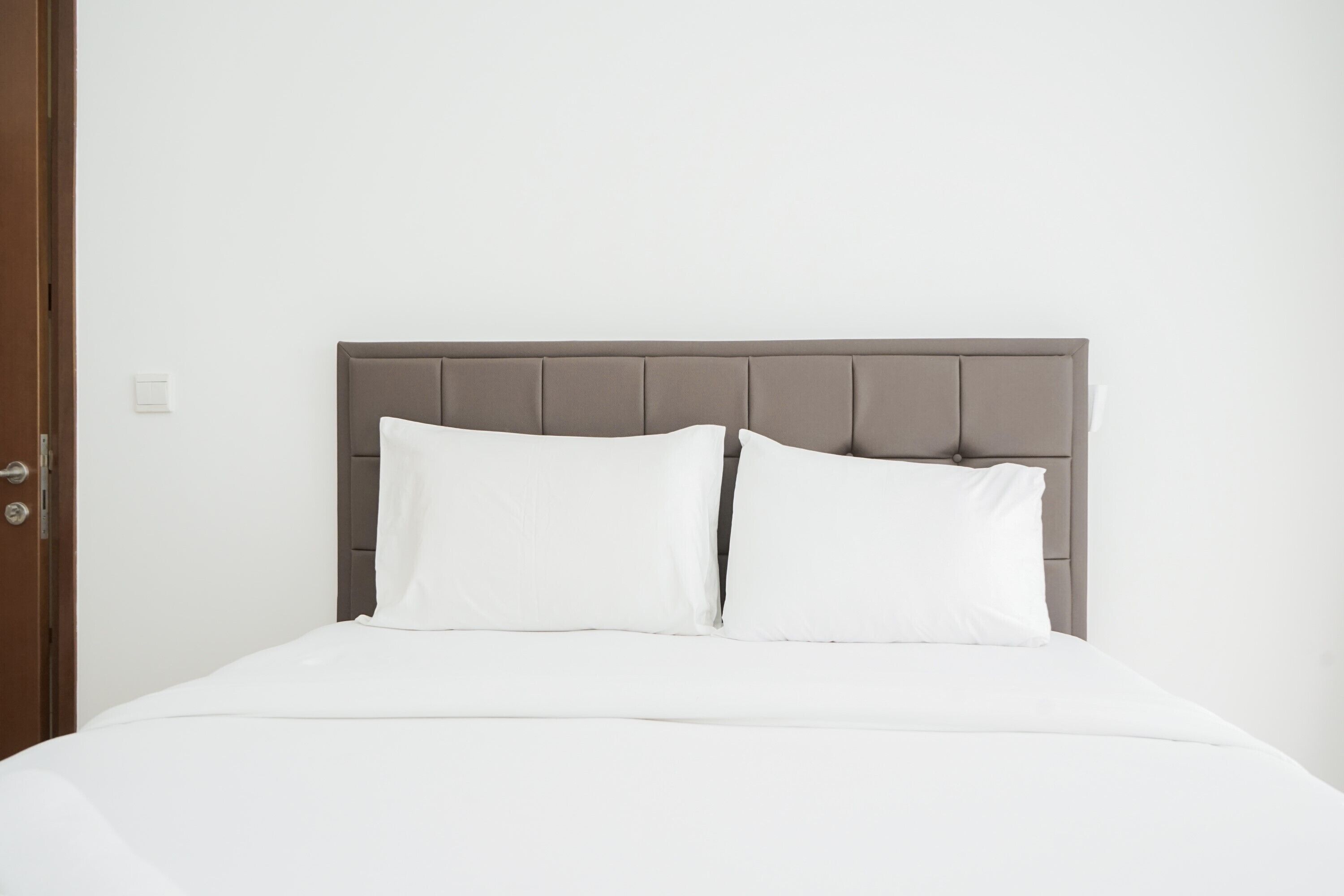 Cama com cabeceira cinzenta e duas almofadas brancas.
