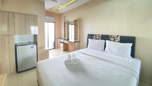 Quarto de hotel com cama, escrivaninha e cozinha compacta.