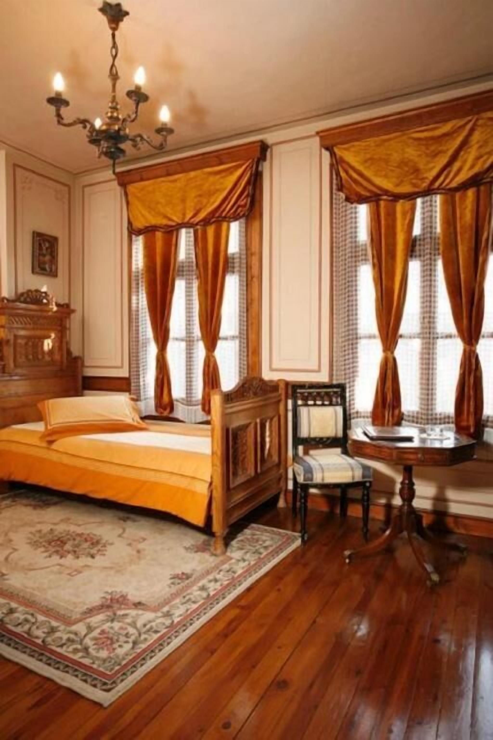 Quarto tradicional com cama de madeira, lustre, escrivaninha e cortinas.
