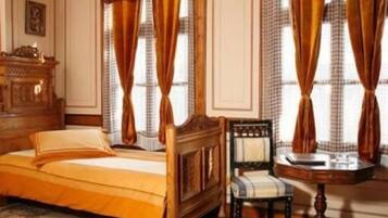 Quarto tradicional com cama de madeira, lustre, escrivaninha e cortinas.