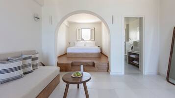 Quarto moderno com uma cama, uma mesinha com uma travessa de fruta e um banheiro visível por um arco.