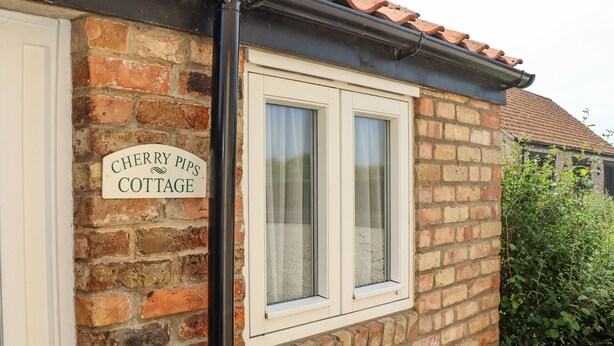 Uma casa de campo de tijolos com uma placa que diz 'Cherry Pips Cottage'.