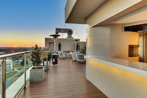 Terraço no telhado com deck de madeira, área de estar externa e vista para o pôr do sol.