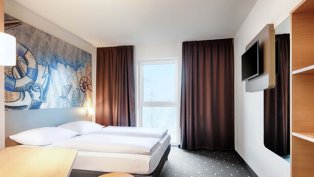 Quarto de hotel com cama, escrivaninha, cadeira, televisão e uma grande pintura abstrata na parede.
