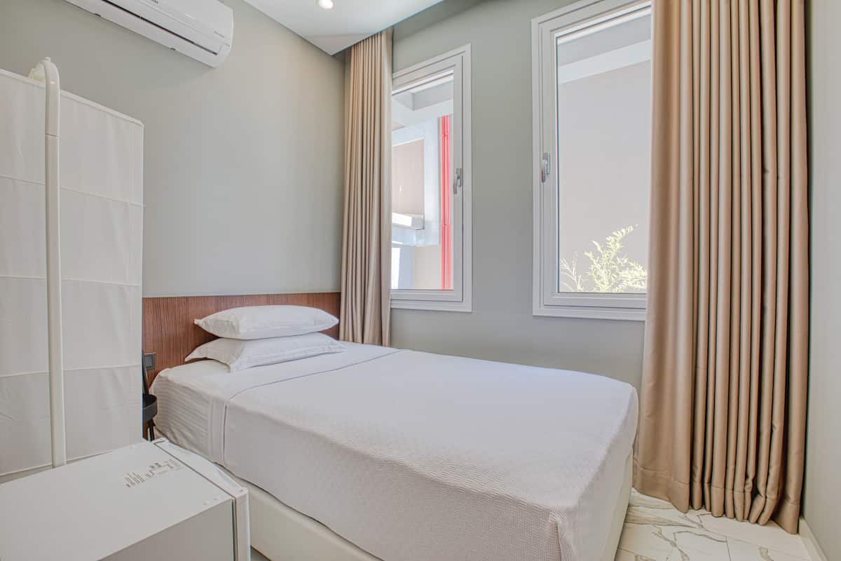 Quarto de hotel bem arrumado com cama, mesa de cabeceira e janela com cortinas.
