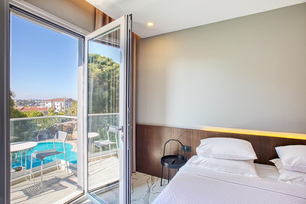 Quarto de hotel com uma grande porta de vidro deslizante que dá para uma varanda com piscina e cadeiras.