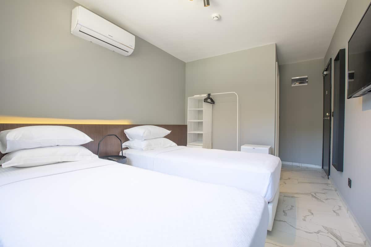Quarto de hotel com duas camas, chuveiro, TV e ar condicionado.