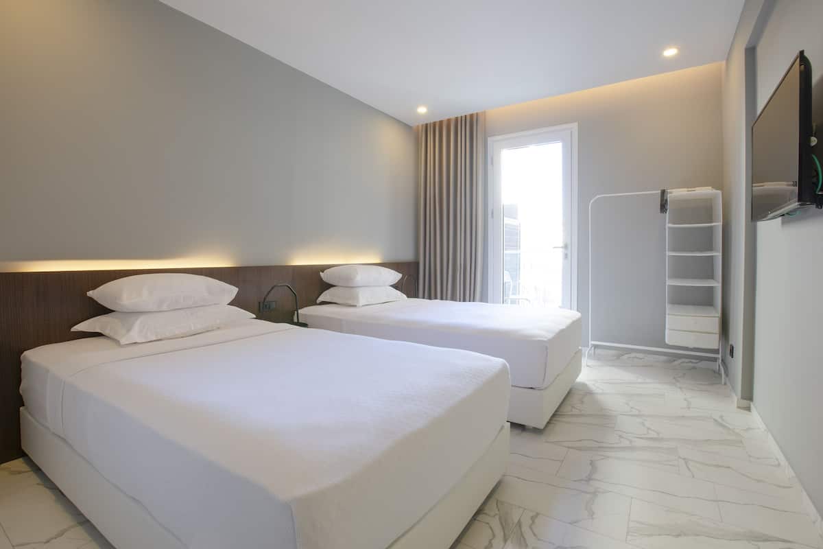 Quarto de hotel moderno com duas camas, uma janela grande com cortinas, uma estante embutida e piso de mármore.