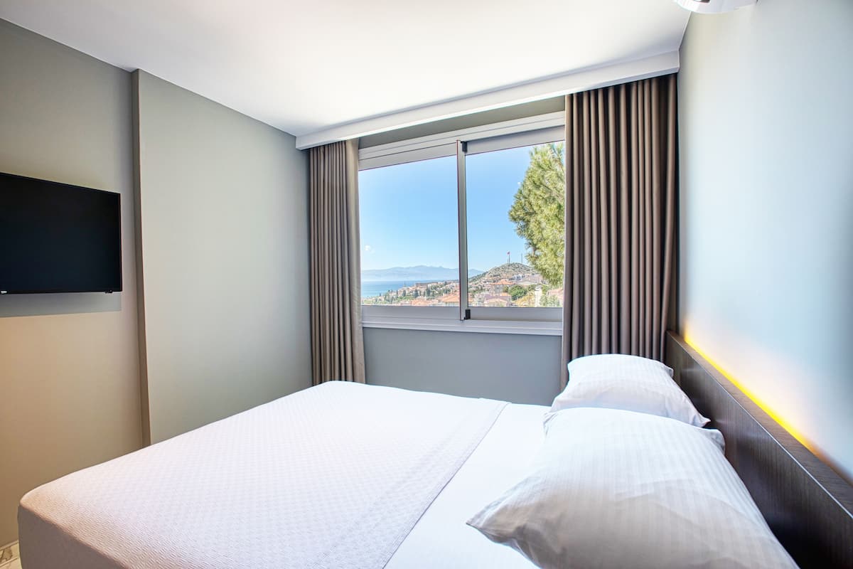 Quarto de hotel com uma cama grande, televisão de tela plana na parede e uma janela com cortinas.
