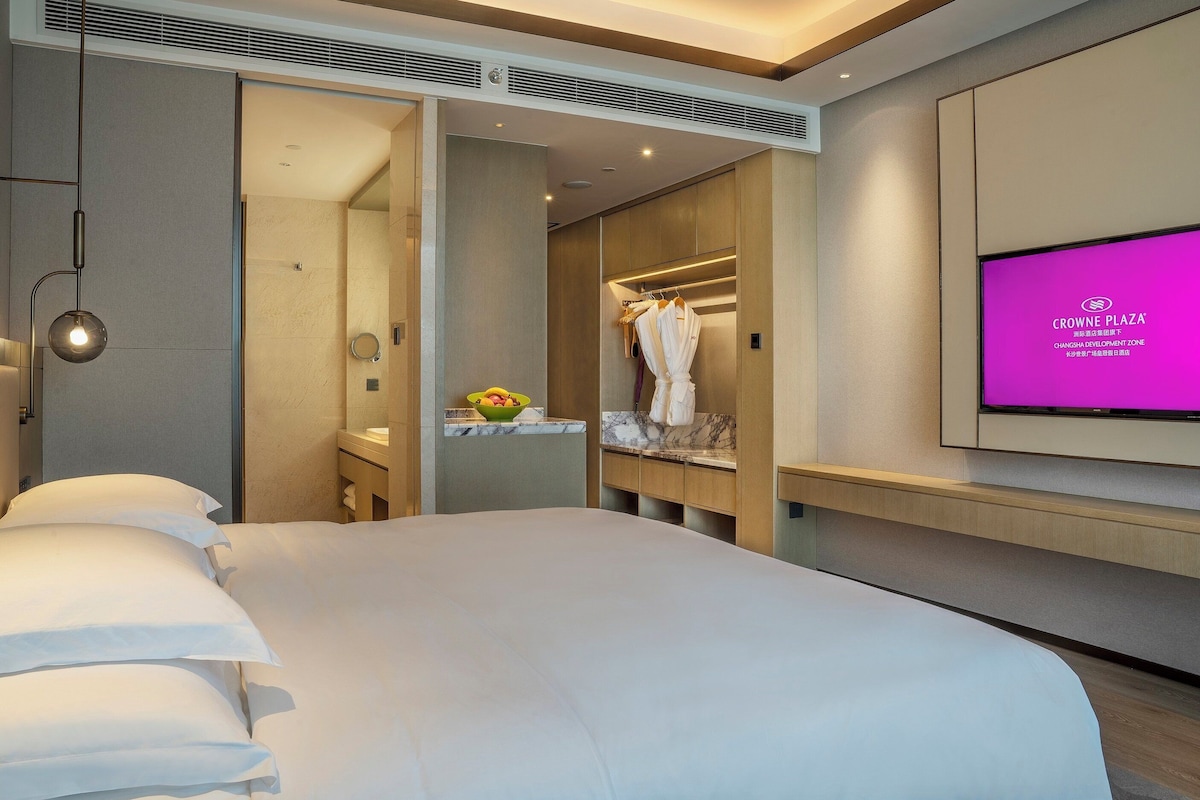 Quarto de hotel com cama, televisão, roupão e espelho.