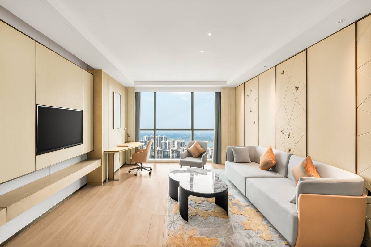 Uma sala de estar moderna com uma televisão grande, um sofá, uma mesa de centro e vista para a cidade através de amplas janelas.