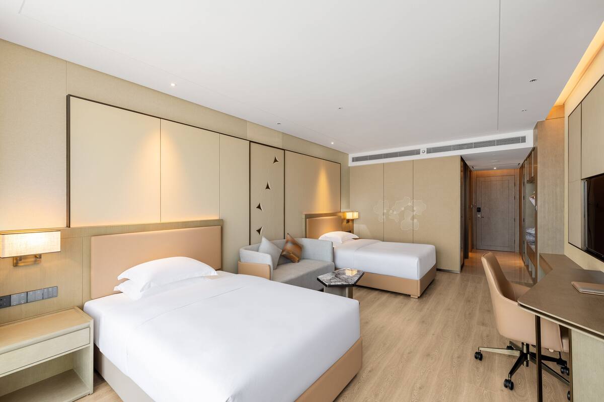 Quarto de hotel com duas camas, uma mesa, uma cadeira e uma televisão.