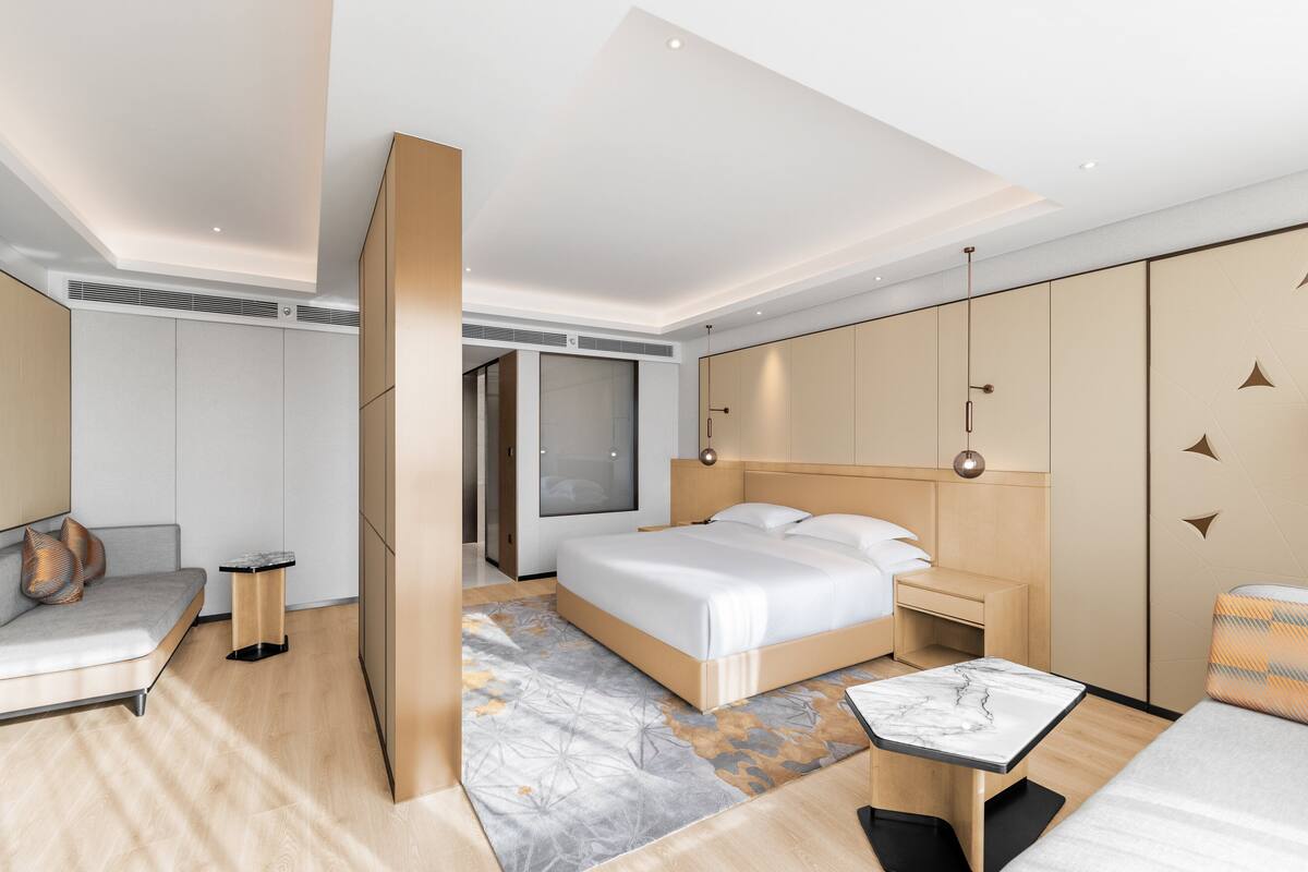 Quarto de hotel moderno com uma cama grande, um sofá, uma mesa pequena e uma escrivaninha.