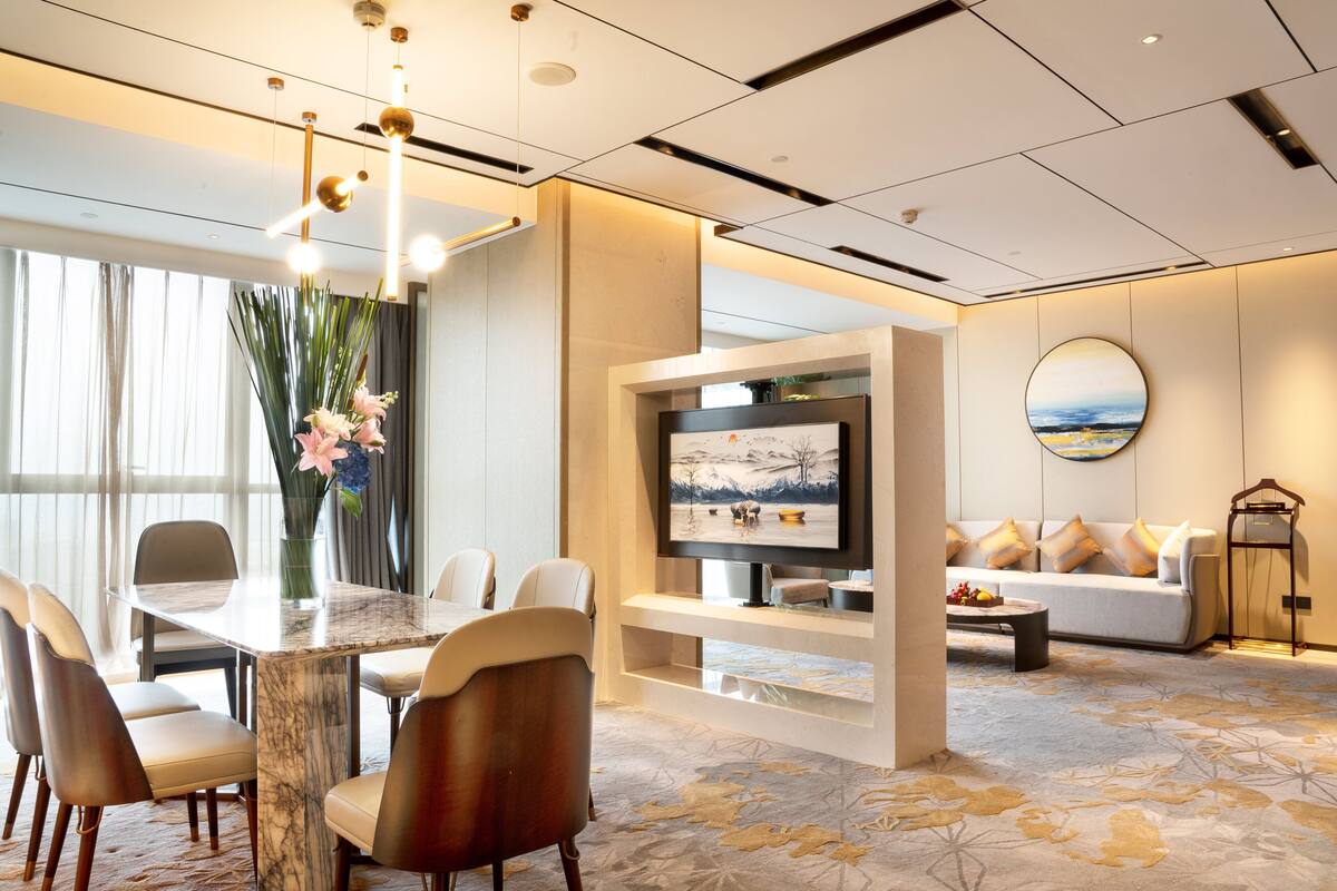 Quarto de hotel moderno com área de refeições, sala de estar e uma televisão grande.