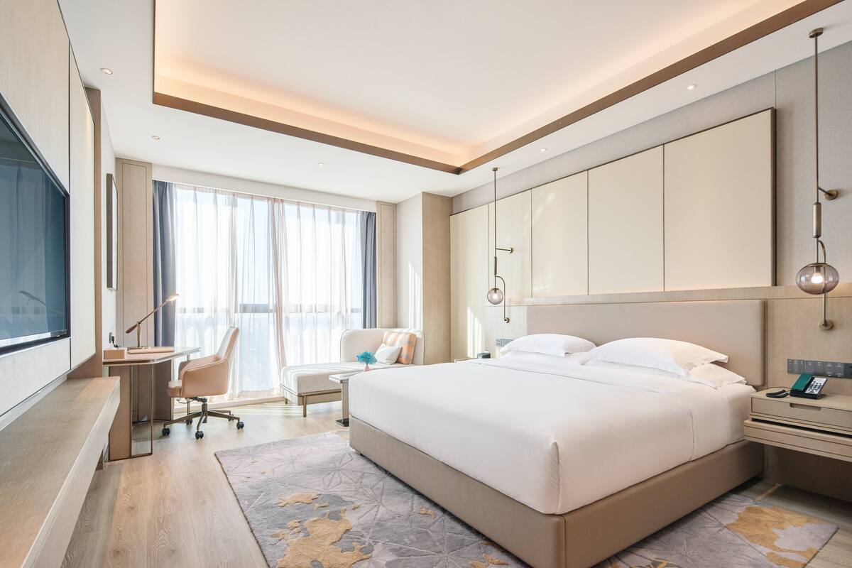 Quarto de hotel moderno com uma cama grande, uma escrivaninha, uma cadeira e uma televisão.