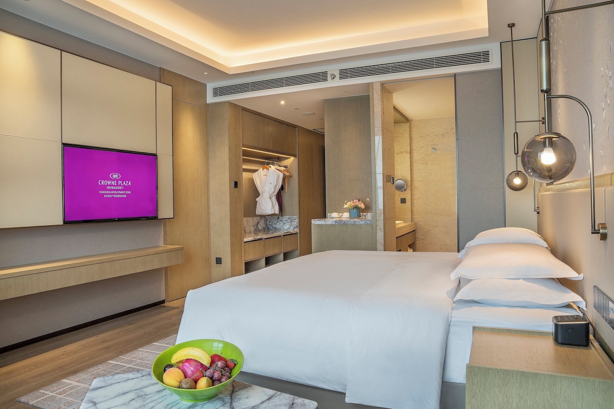 Quarto de hotel com cama, televisão, banheiro e uma cesta de frutas.