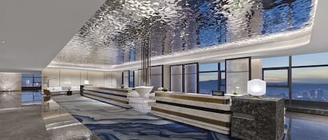 Um lobby moderno de hotel com teto espelhado, balcão de recepção e grandes janelas com vista para a cidade.